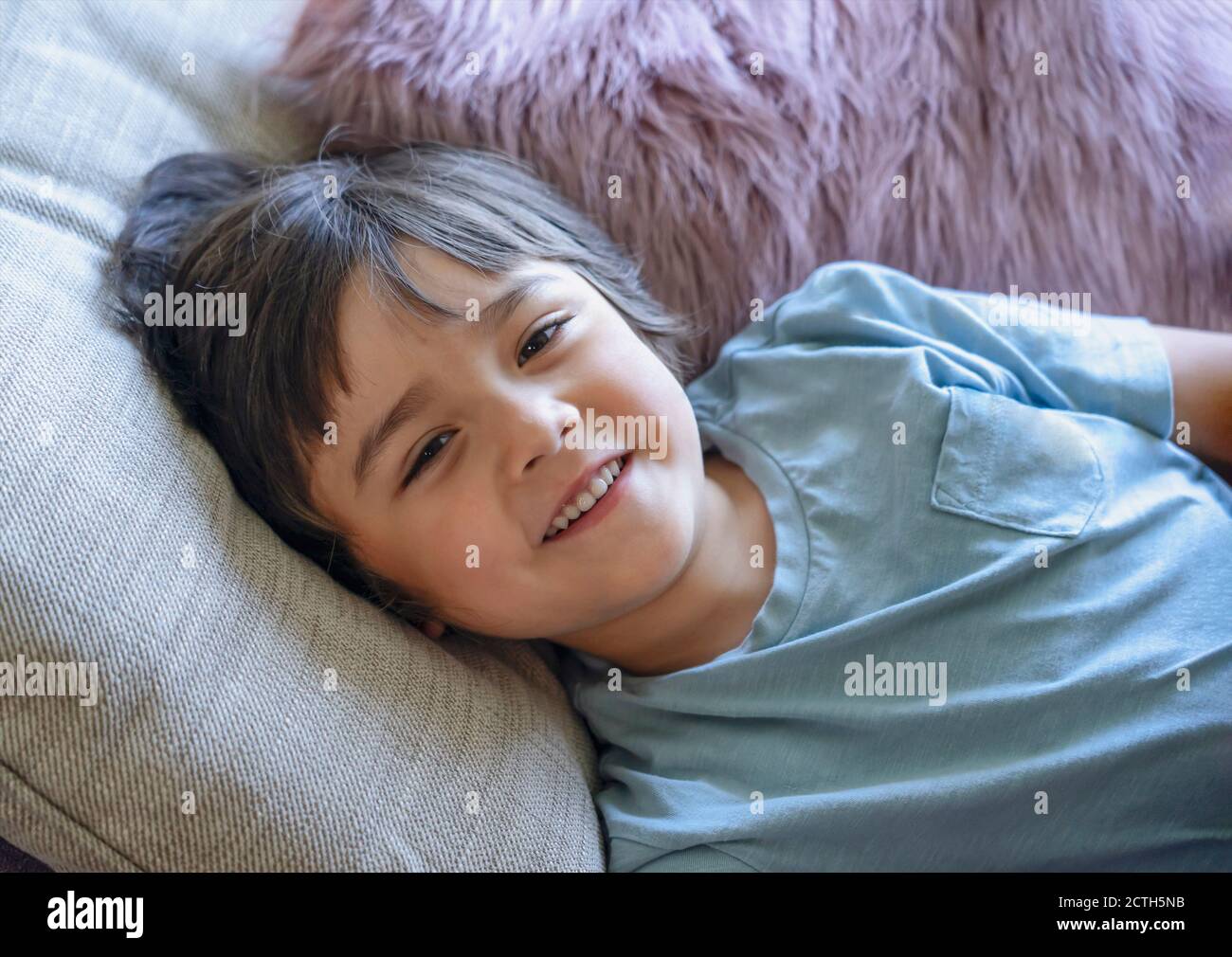 Healthy kid with smiling face lying head down on fuffy cushion, Happy ...