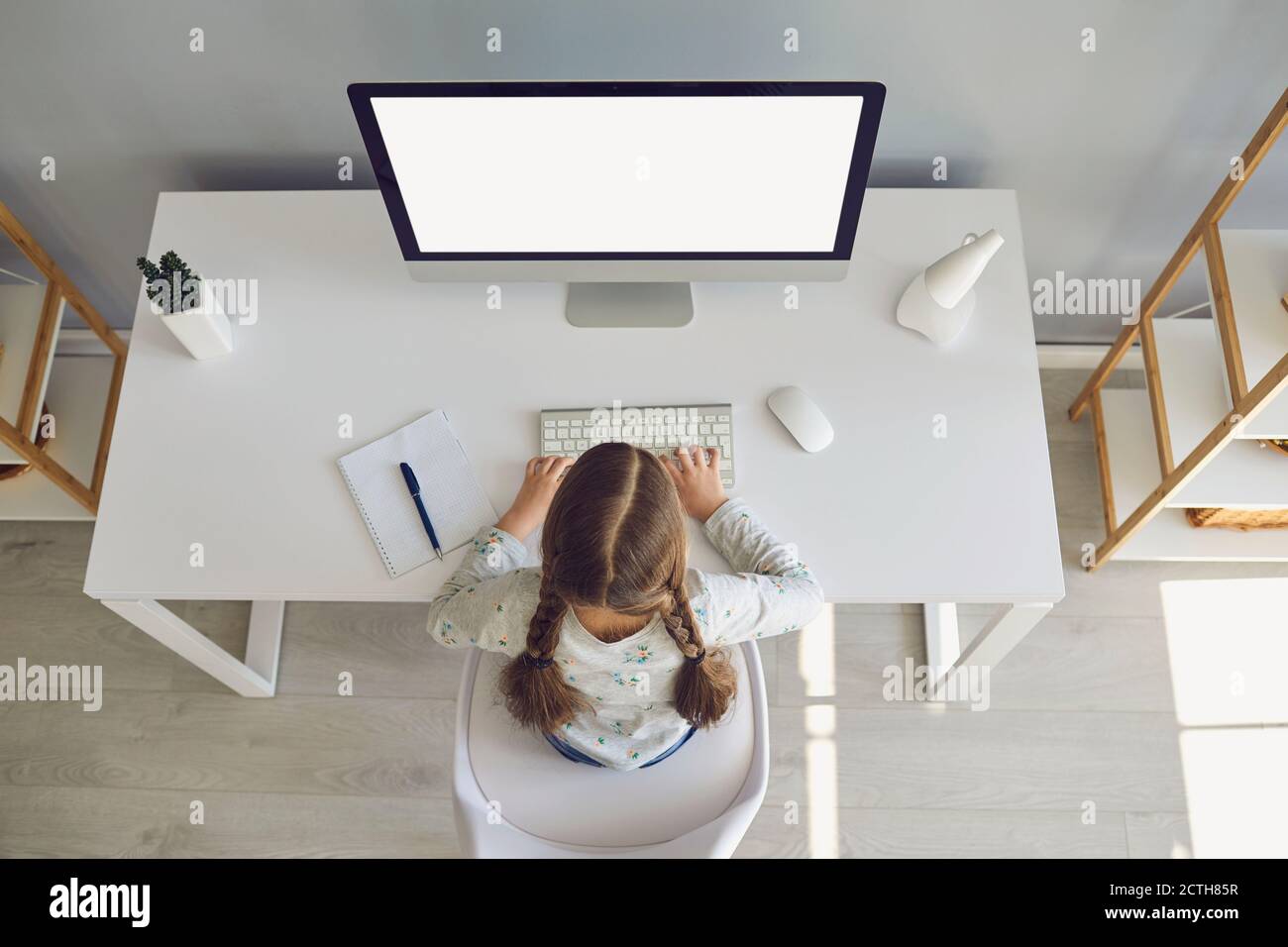 Girl sitting at table with computer, watching online lesson and typing ...
