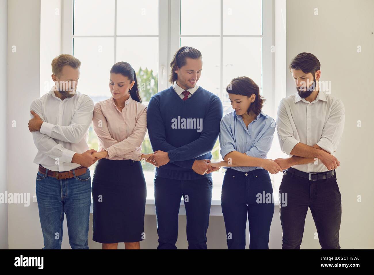 Positive office employees standing in a row holding hands supporting ...