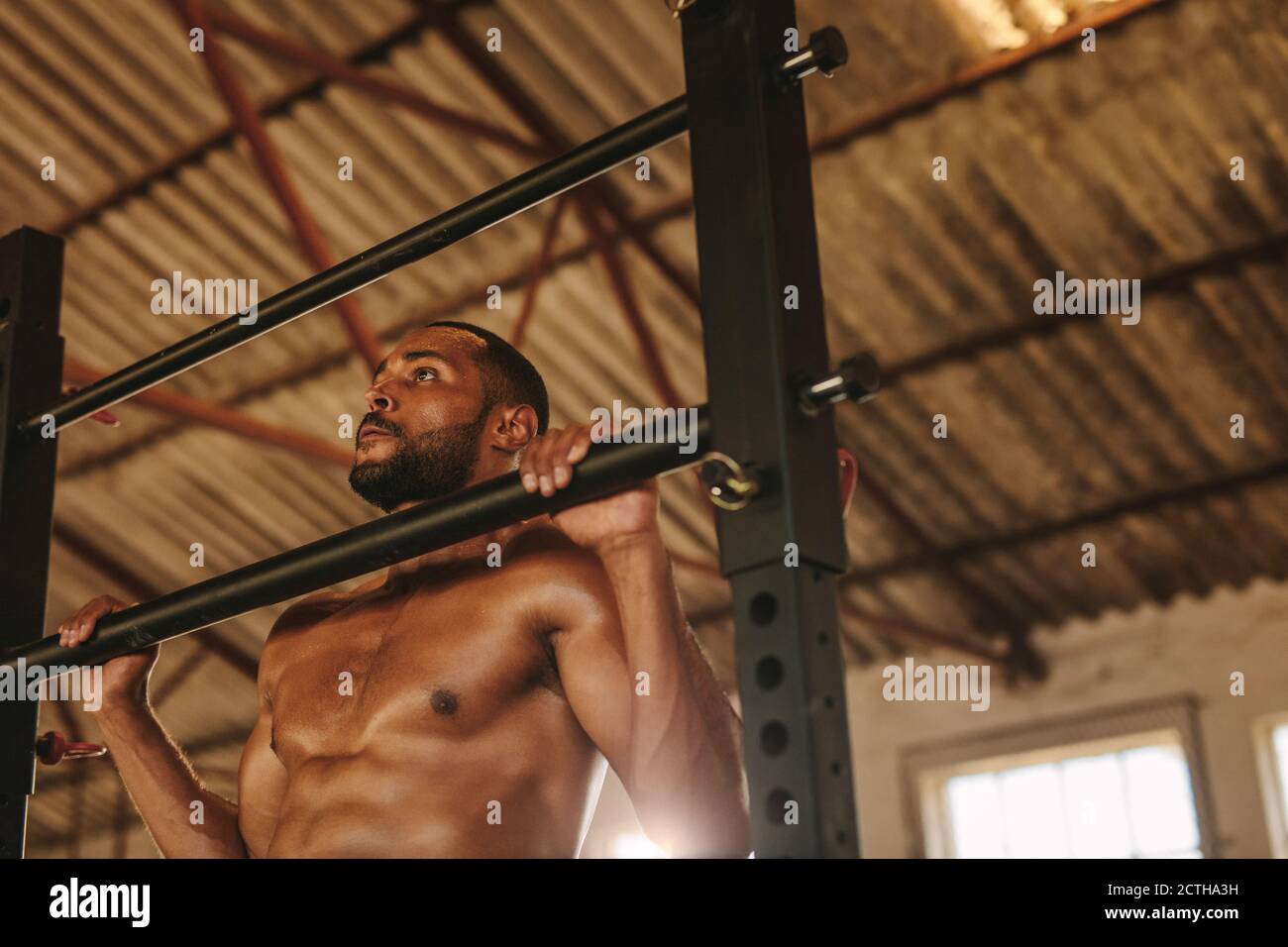 Muscular man doing pull up workout on horizontal bar in fitness studio ...