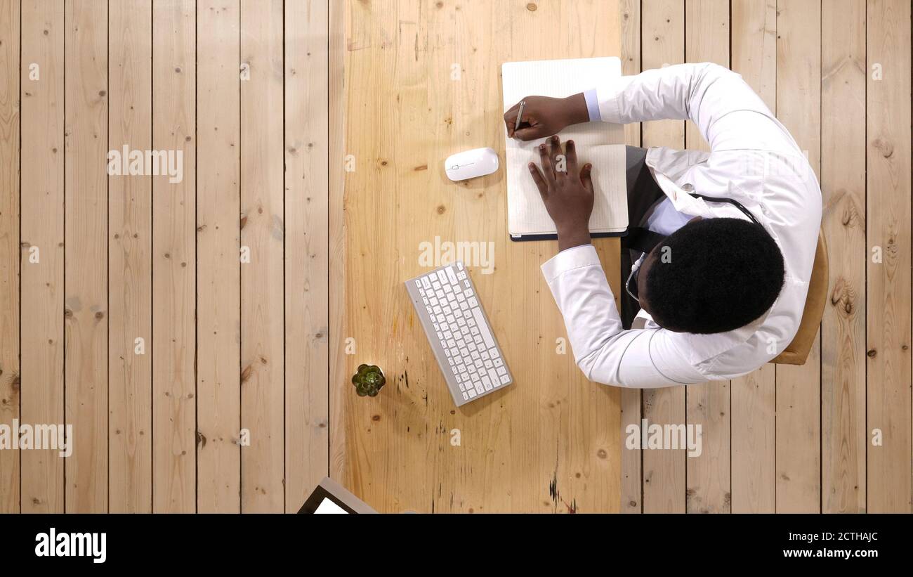 Male doctor writes notes sitting at desk with mess on it Stock Photo ...