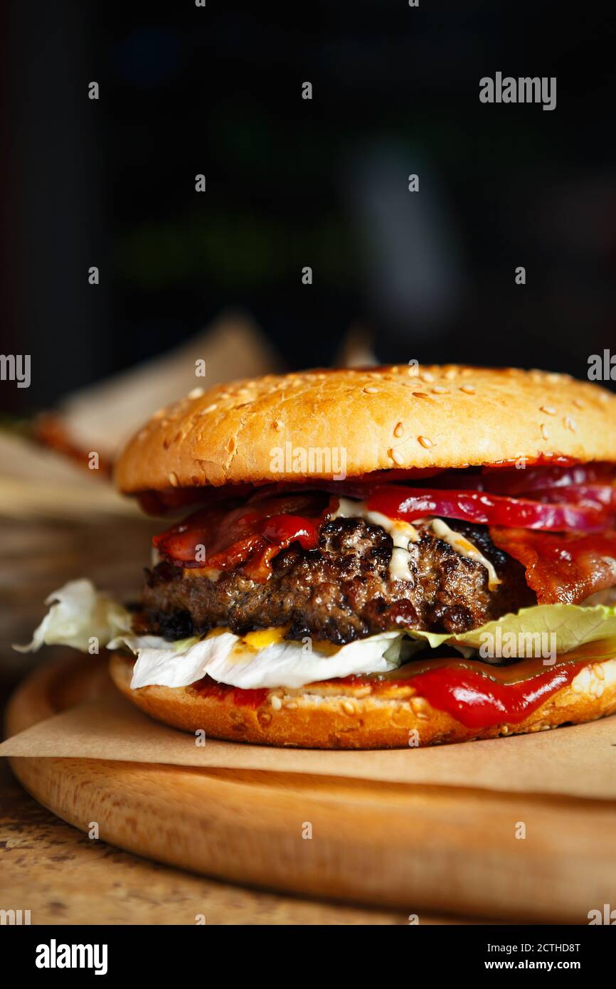 Big fat burger with bacon stripes served on wooden plate on table in ...