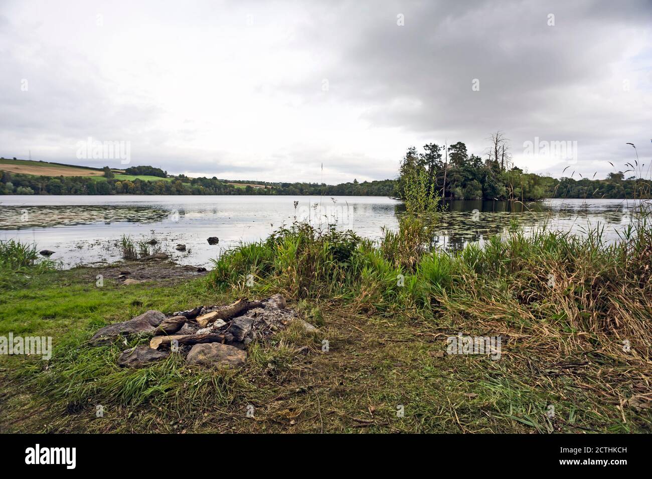 Wild camping site with ashes and logs from burnt out fire in foreground ...