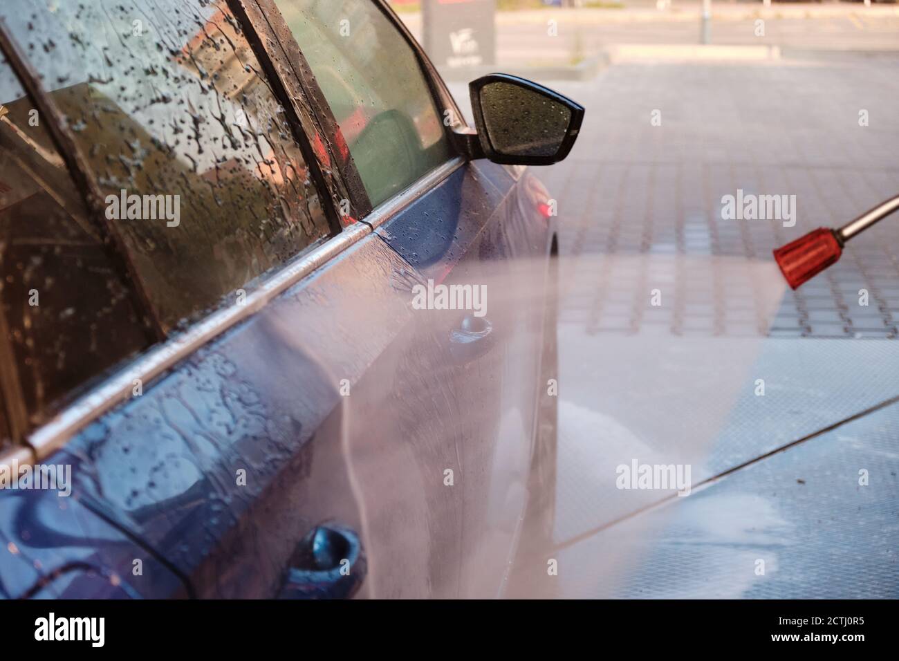 Side view of a blue car washing under high pressure water. Self service ...