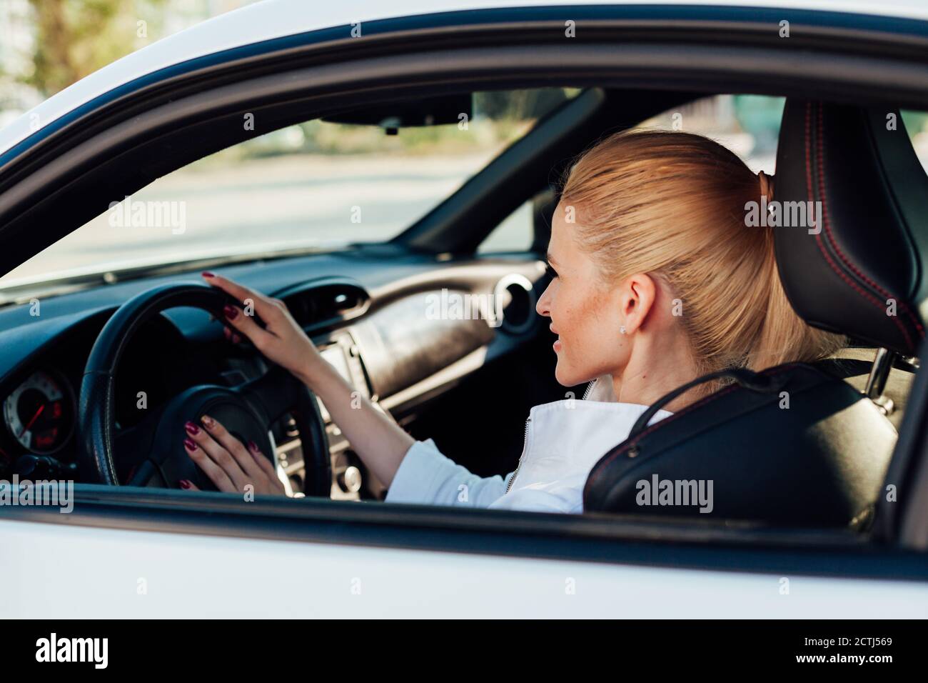 Beautiful female blonde driver behind the wheel of a car on the road ...