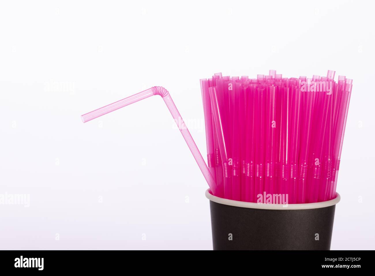 Pink straws in black paper cup on white background. One flexible straw ...