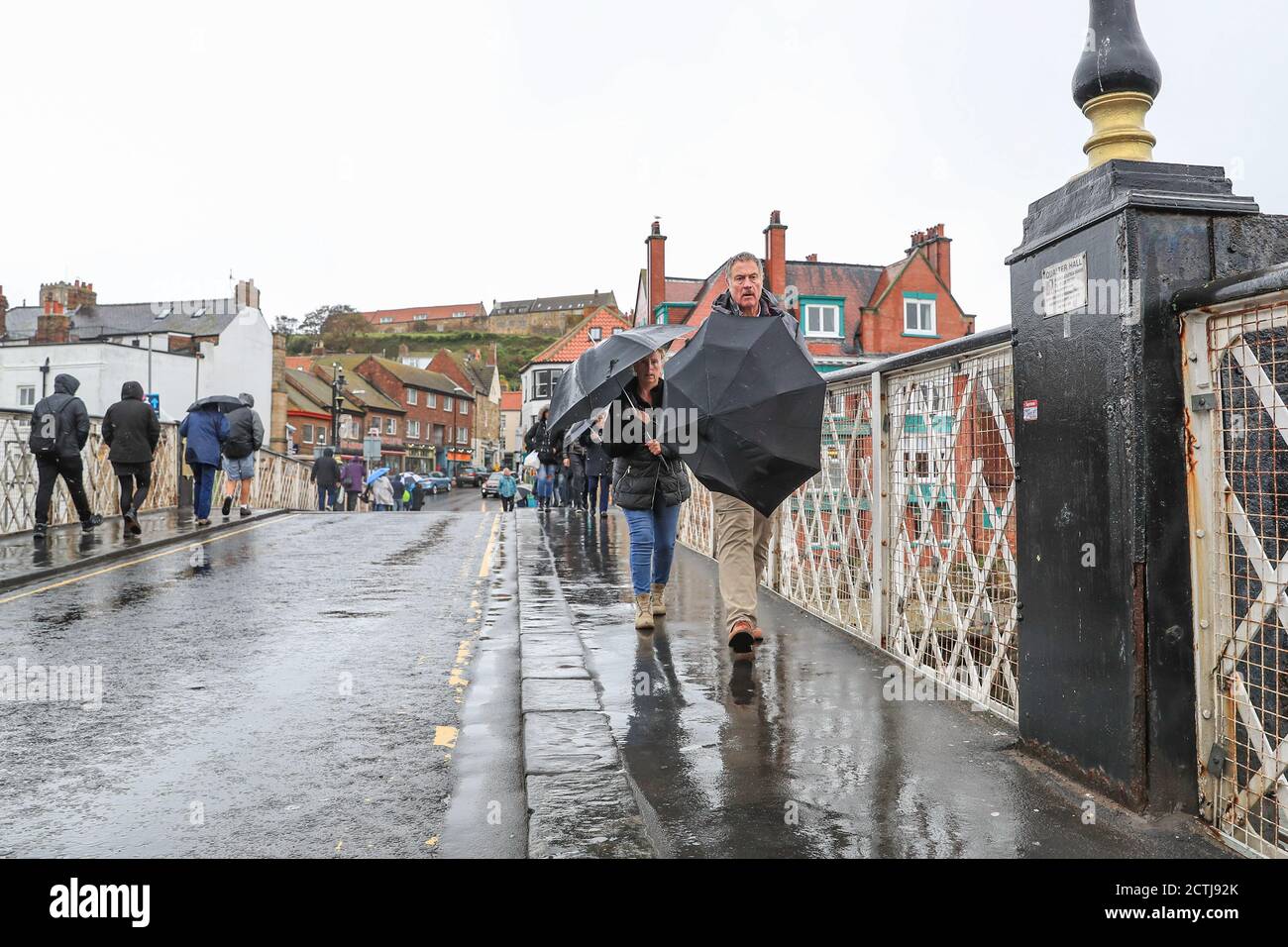 A couple walk over Whitby’s famous swing bridge as the wind and rain ...