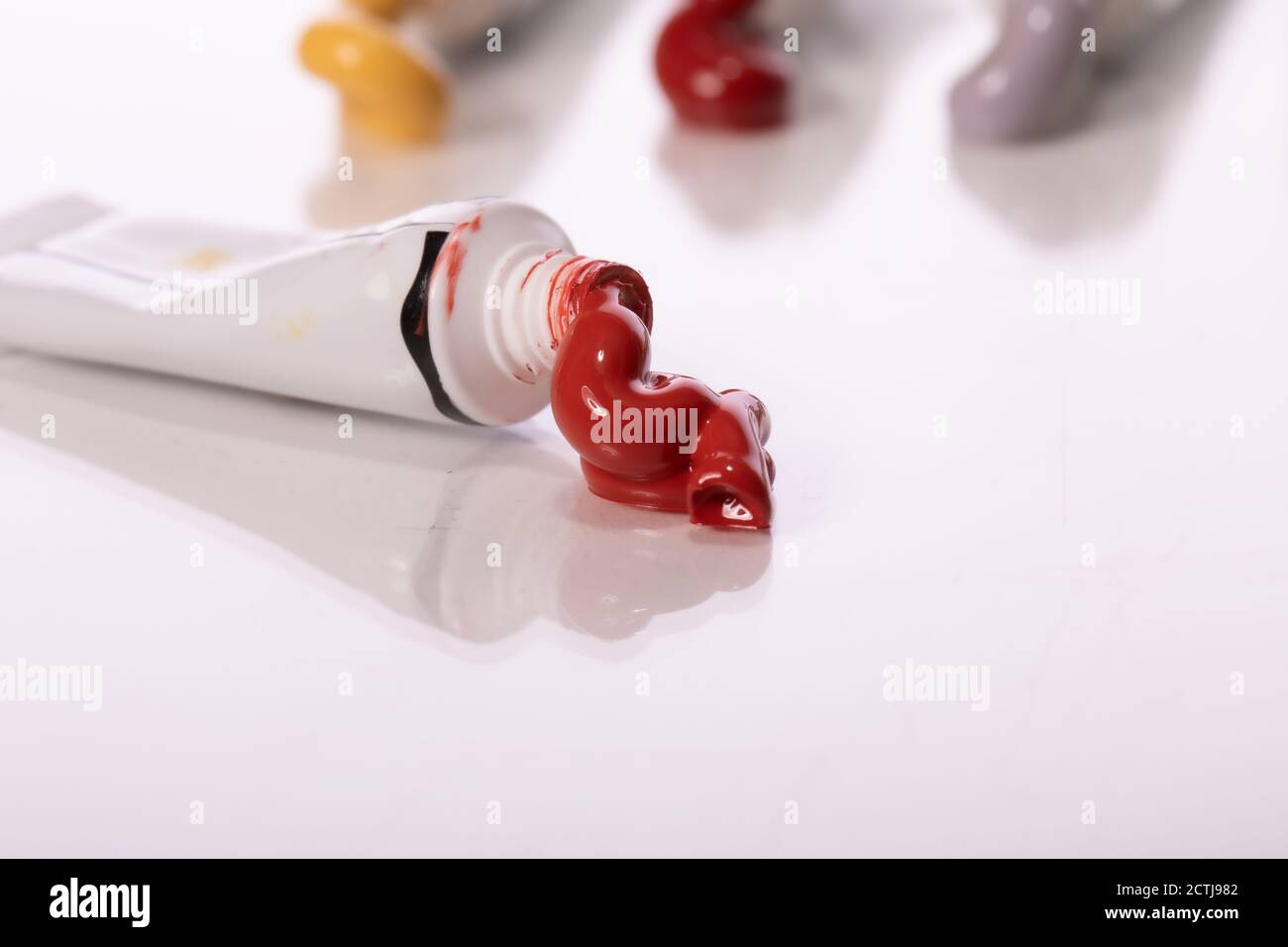 large drop of red glossy paint squeezed out of tube reflected in glass ...