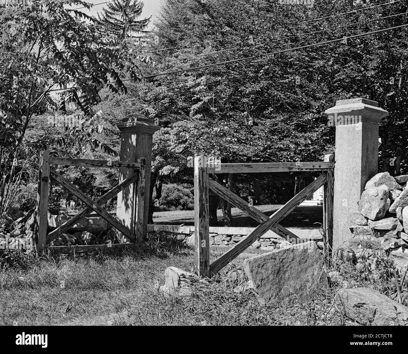 A worn wood gate stands open to an empty pasture from a street ...