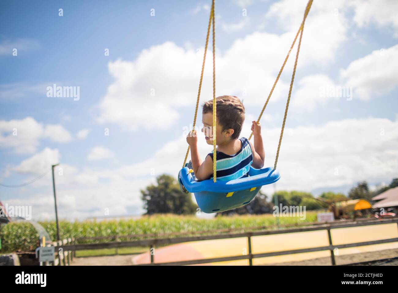 Low angle view of boy swinging outdoors on blue swing at playground ...