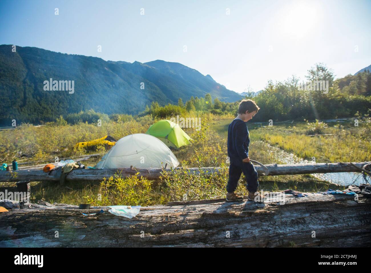 Young boy balancing on fallen log near wilderness campsite, Canada ...