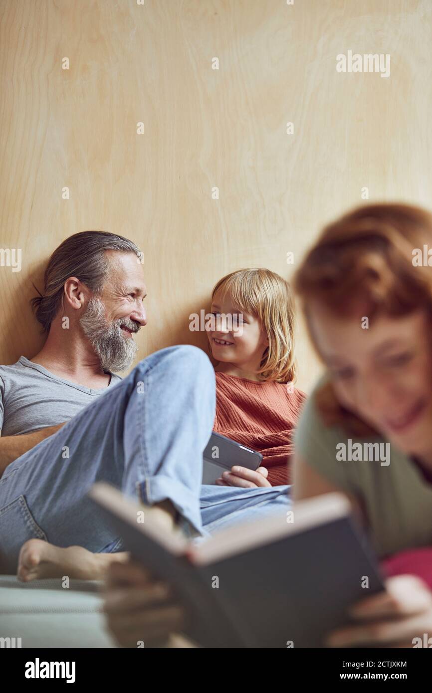 Smiling Father And Daughter Looking At Each Other While Woman Reading