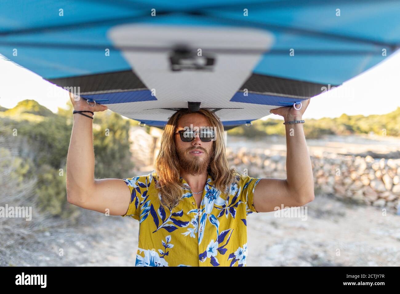 Young man carrying paddleboard on head at beach during sunset Stock ...