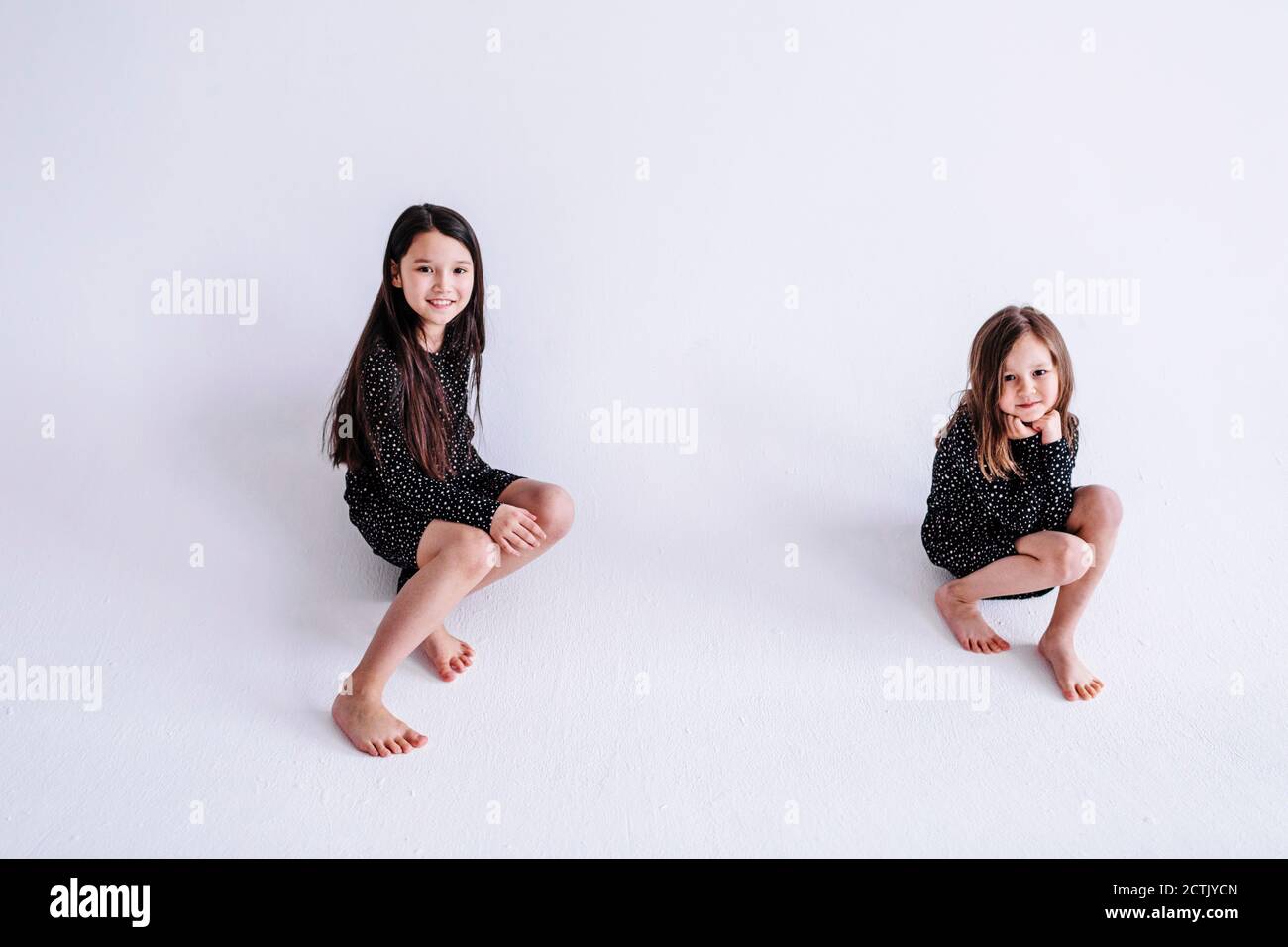 Smiling sisters sitting against white background in studio Stock Photo ...