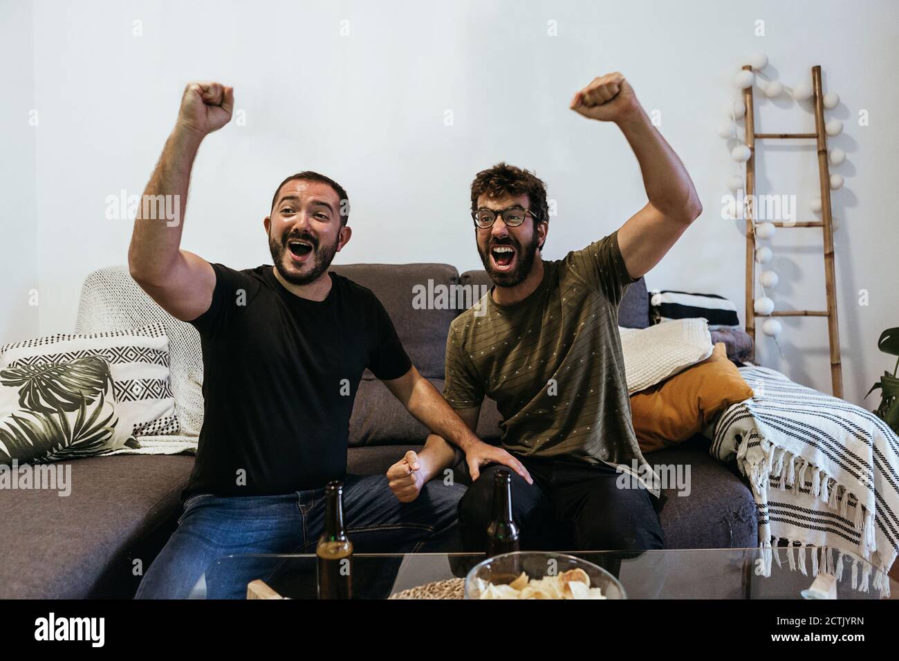Cheerful male spectators screaming while watching sports in living room ...
