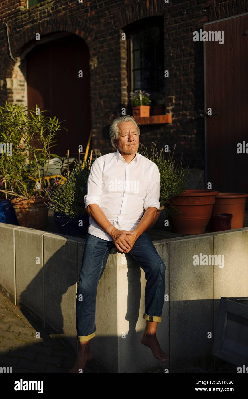Contemplating man sitting on retaining wall while looking away in yard ...