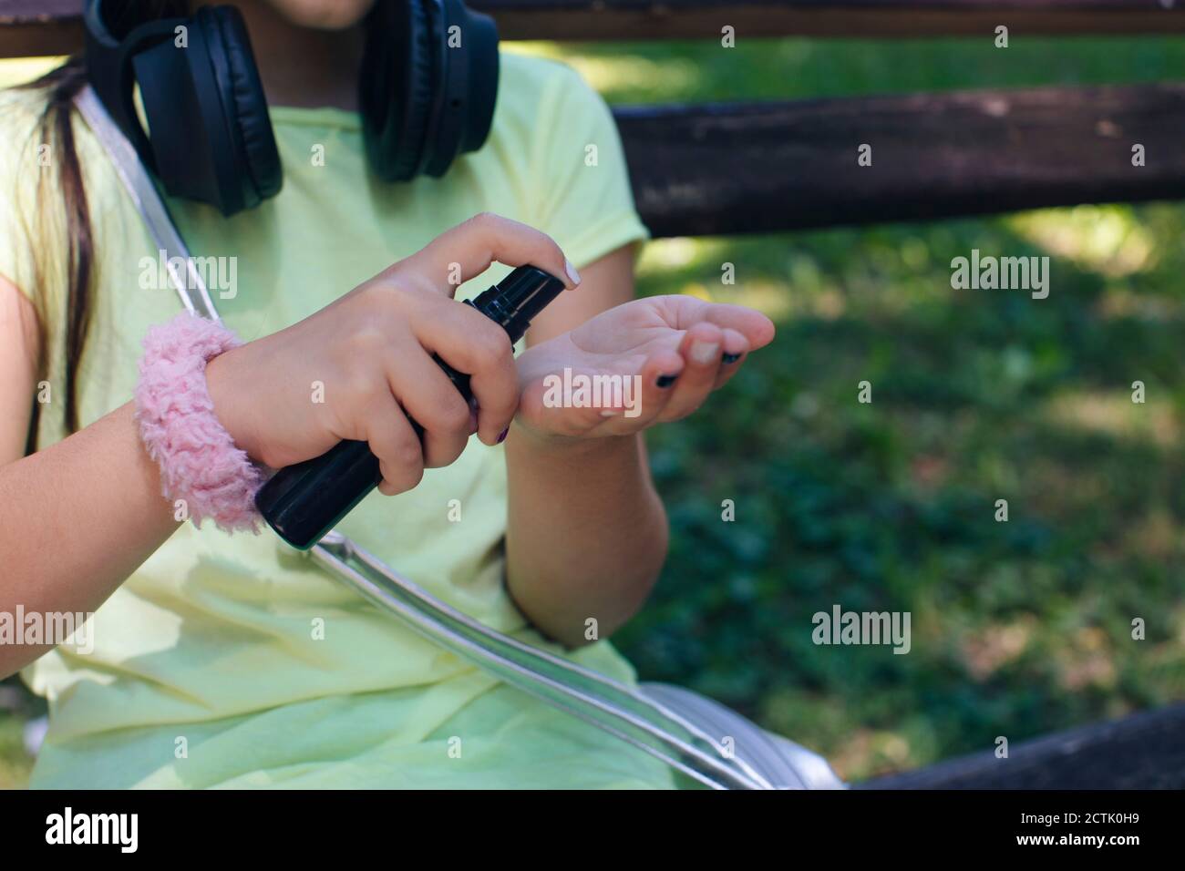 Girl using hand sanitizer while sitting on bench in park Stock Photo ...