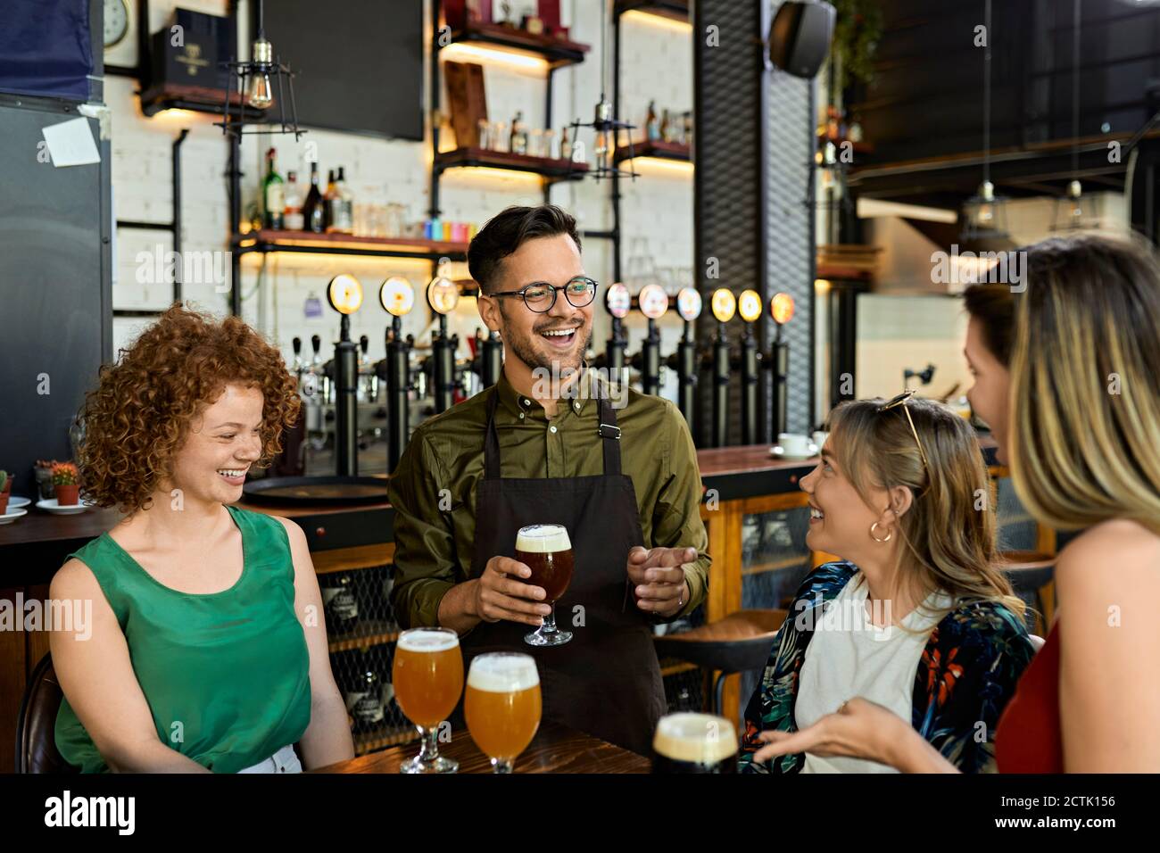 Waiter serving craft beer for female friends in a pub Stock Photo - Alamy