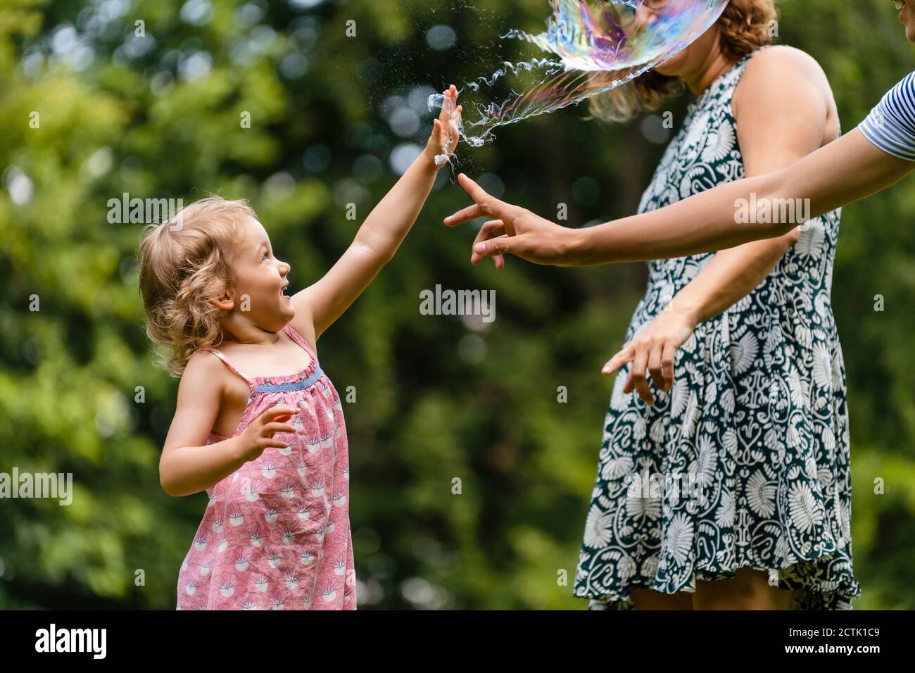 Girl exploding bubble while playing with family at park Stock Photo - Alamy