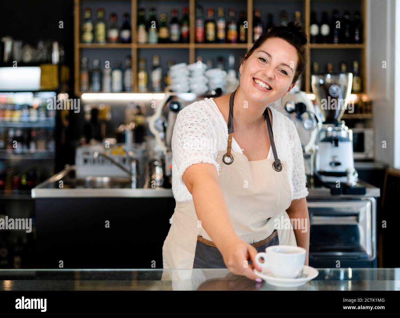 Smiling female owner serving coffee cup on bar counter while working in ...