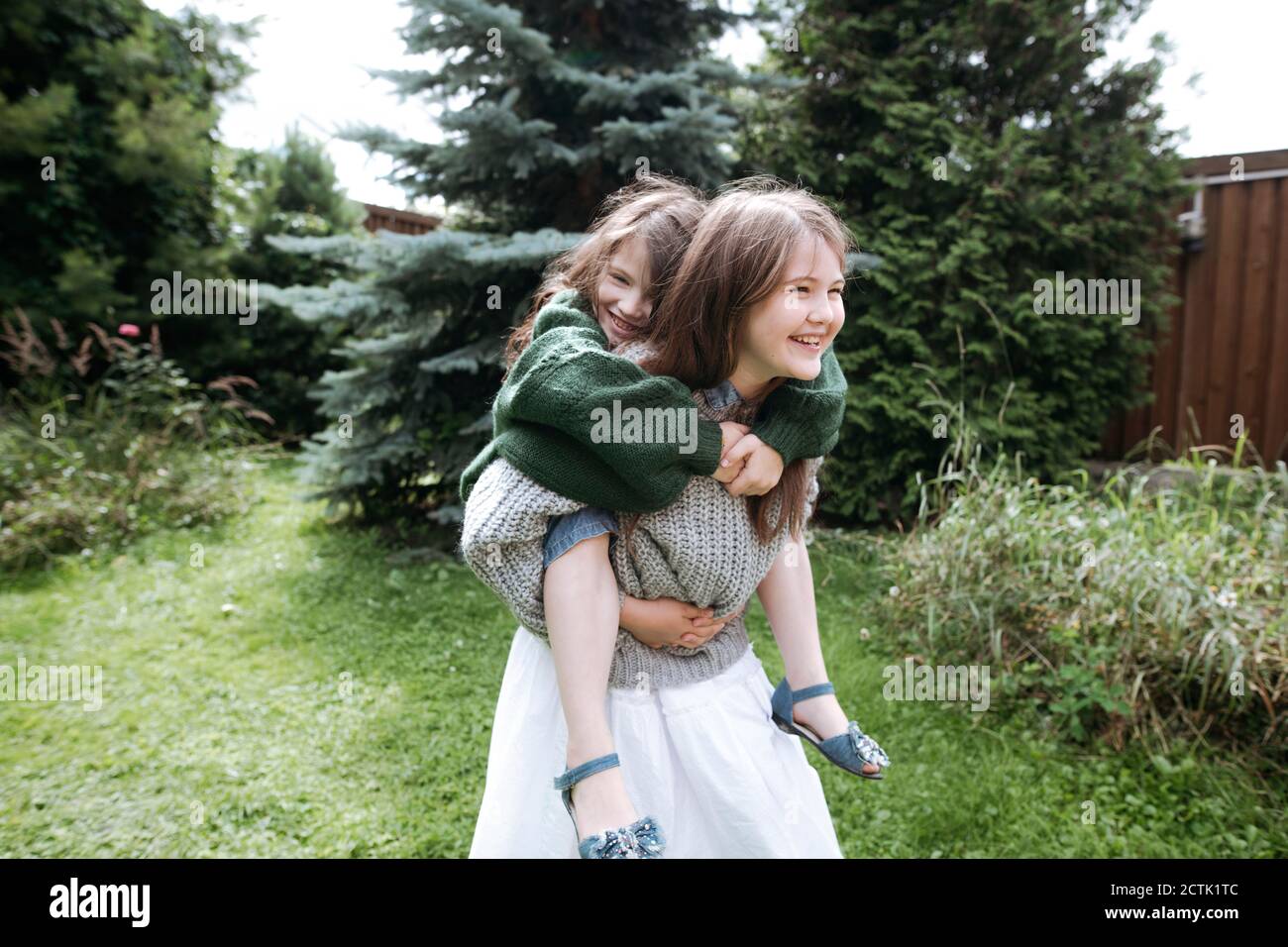 Girl giving piggyback ride sister in back yard Stock Photo - Alamy