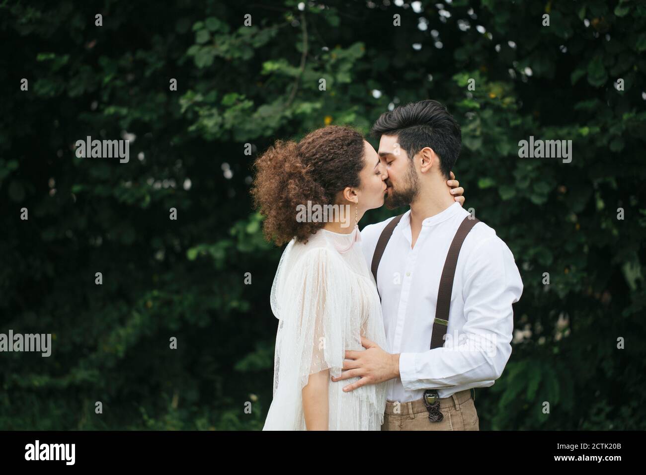 Bride kissing groom while standing at garden Stock Photo - Alamy