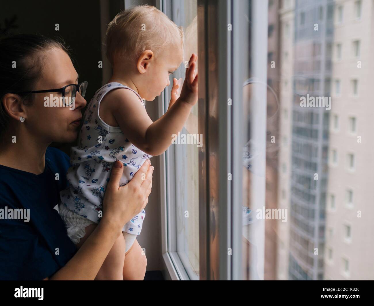 Mother holding baby boy looking through window at home Stock Photo - Alamy