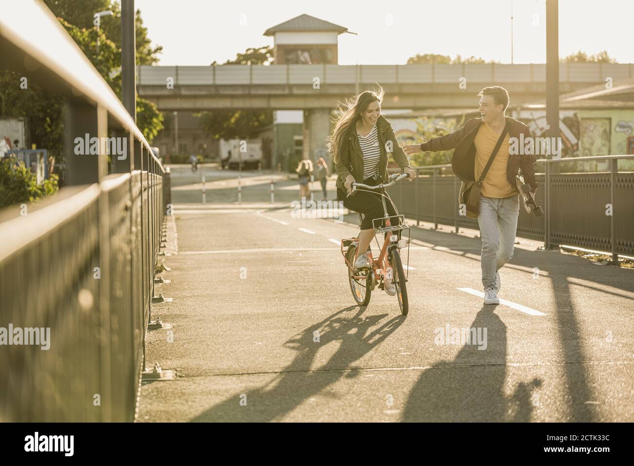 Happy young man running by girlfriend riding bicycle in city during ...