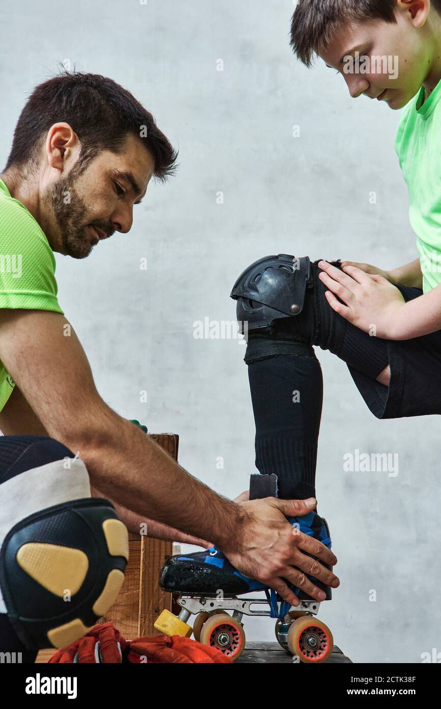 Man helping son wearing roller skate before training Stock Photo - Alamy
