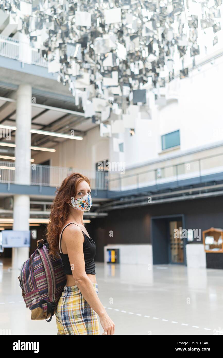 Redhead woman walking indoors while wearing protective face mask Stock ...
