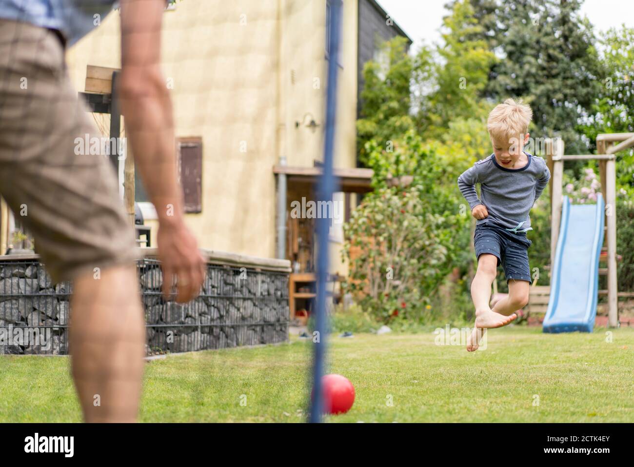 Blond boy kicking ball while playing soccer with father at back yard ...