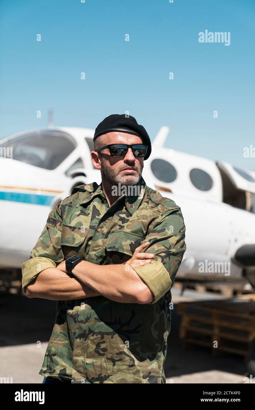 Army soldier standing with arms crossed against airplane on sunny day ...
