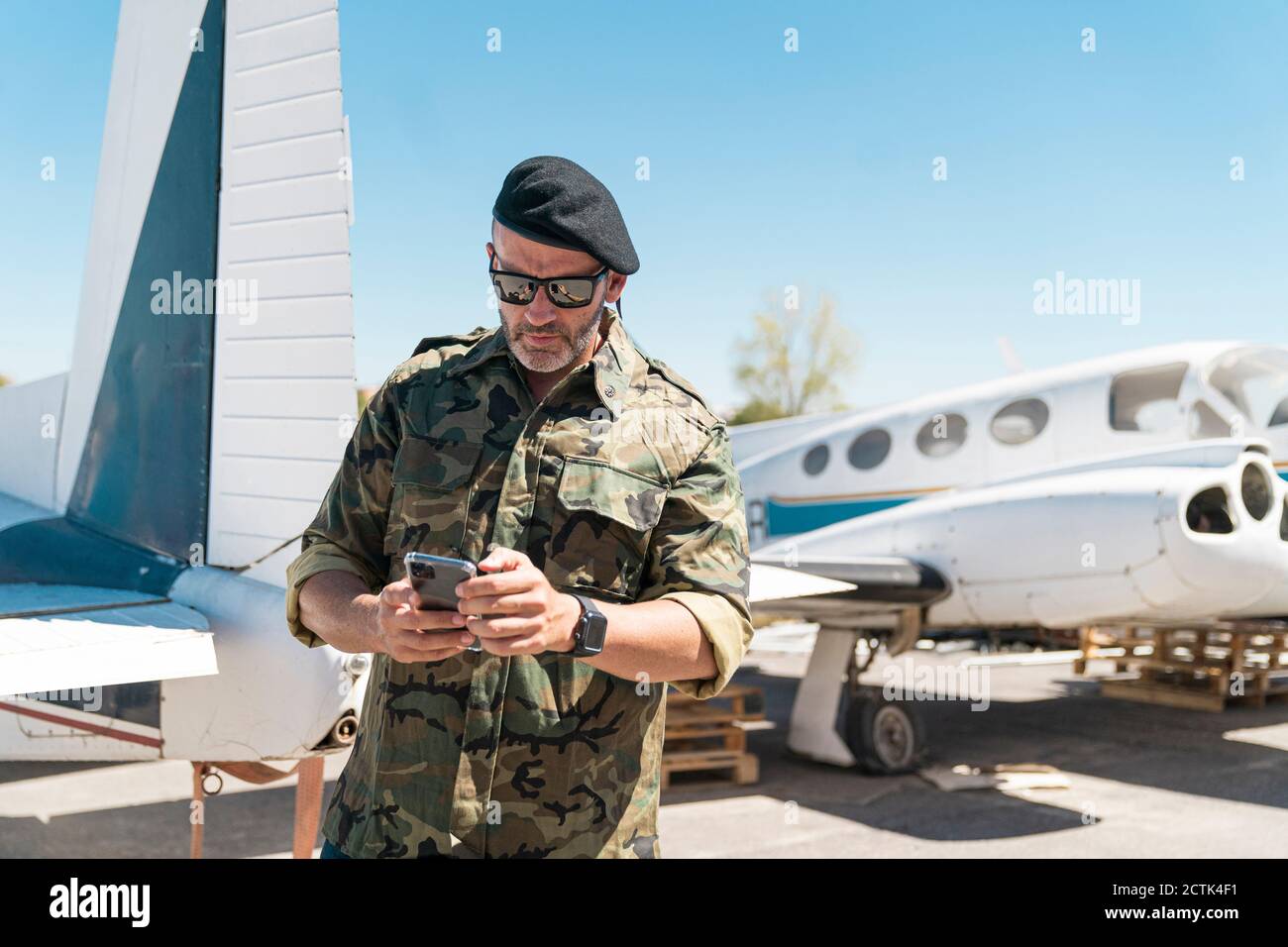 Confident army soldier text messaging on smart phone while standing ...