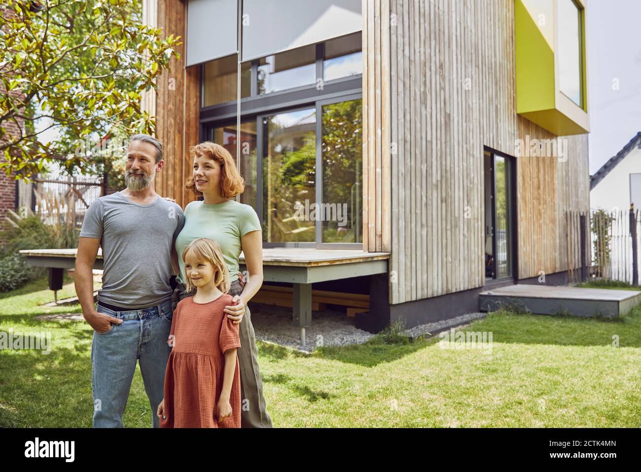 Smiling family looking away while posing against tiny house in yard ...