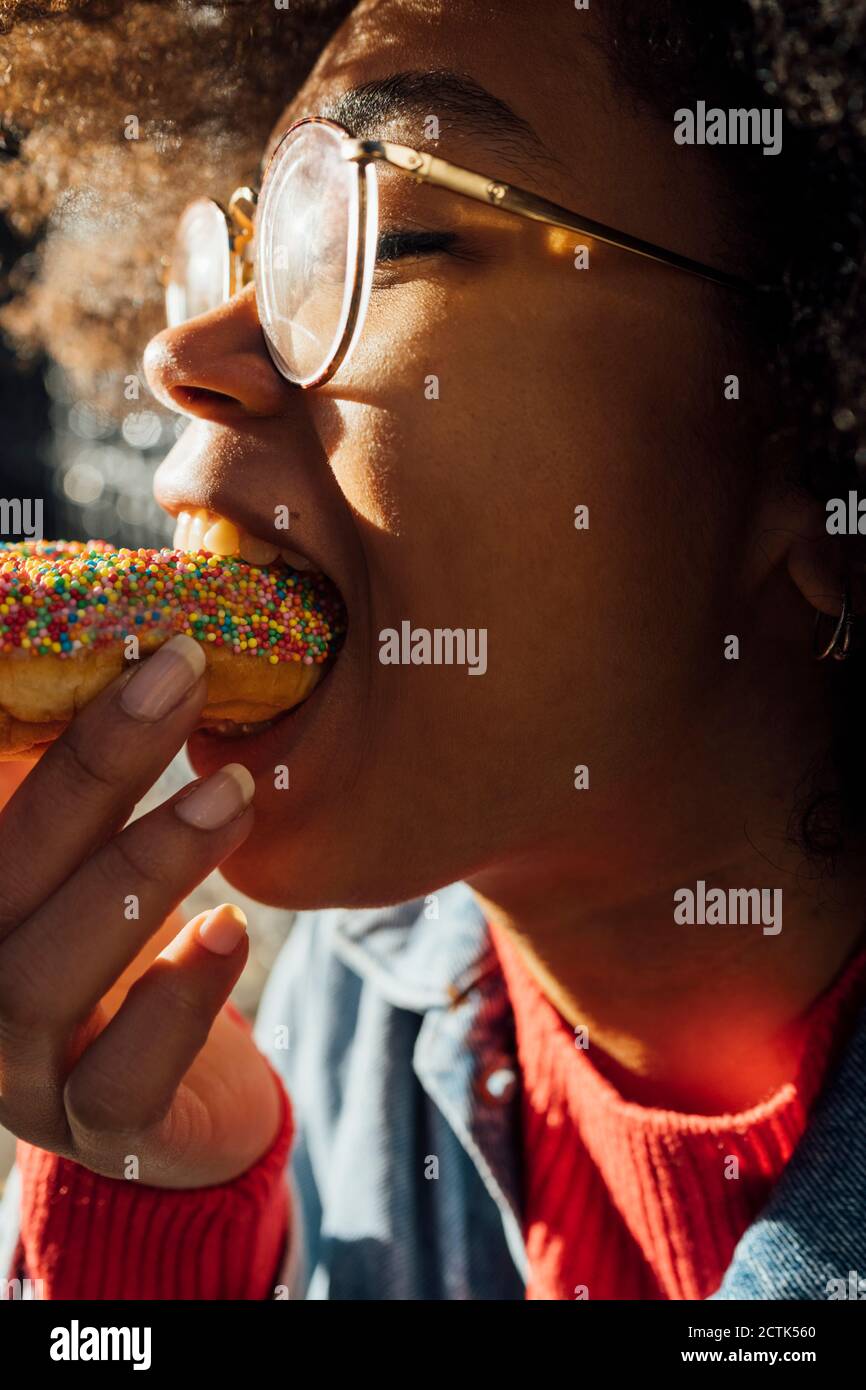Close-up of young woman wearing eyeglasses eating donut Stock Photo - Alamy