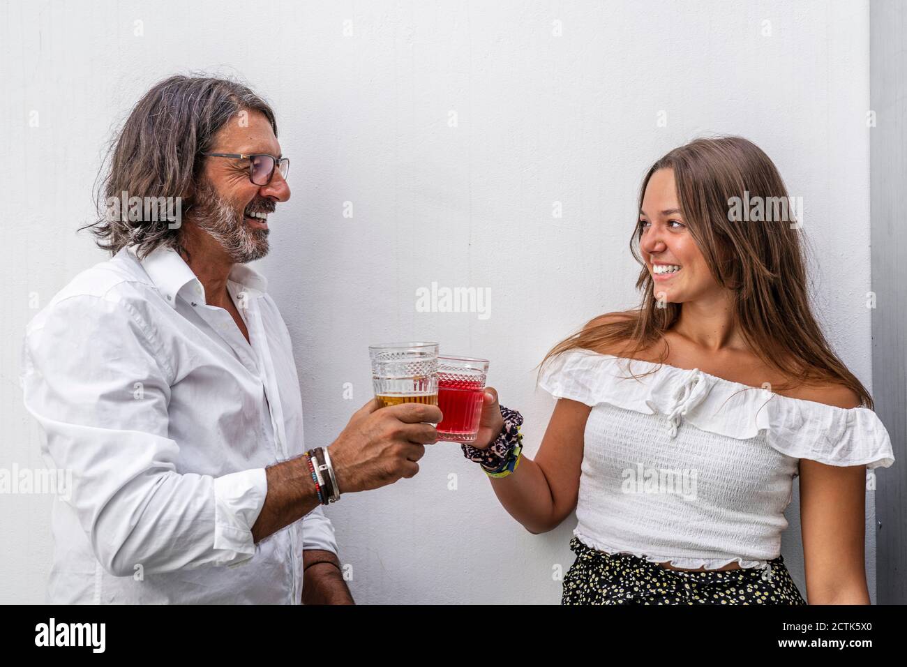 Smiling man toasting drinks with daughter while standing against wall ...