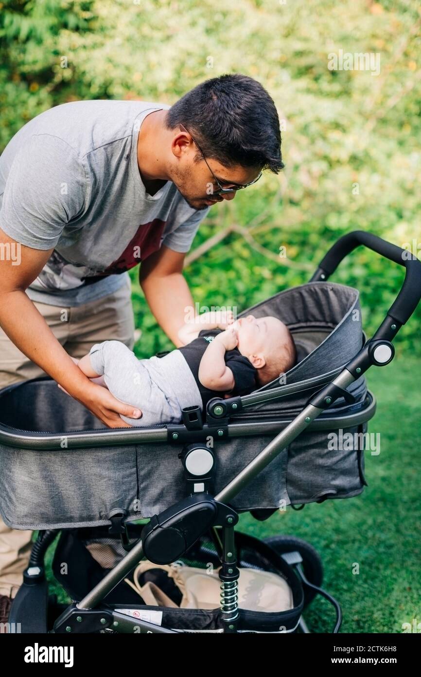 Young man putting baby boy in carriage at park Stock Photo - Alamy