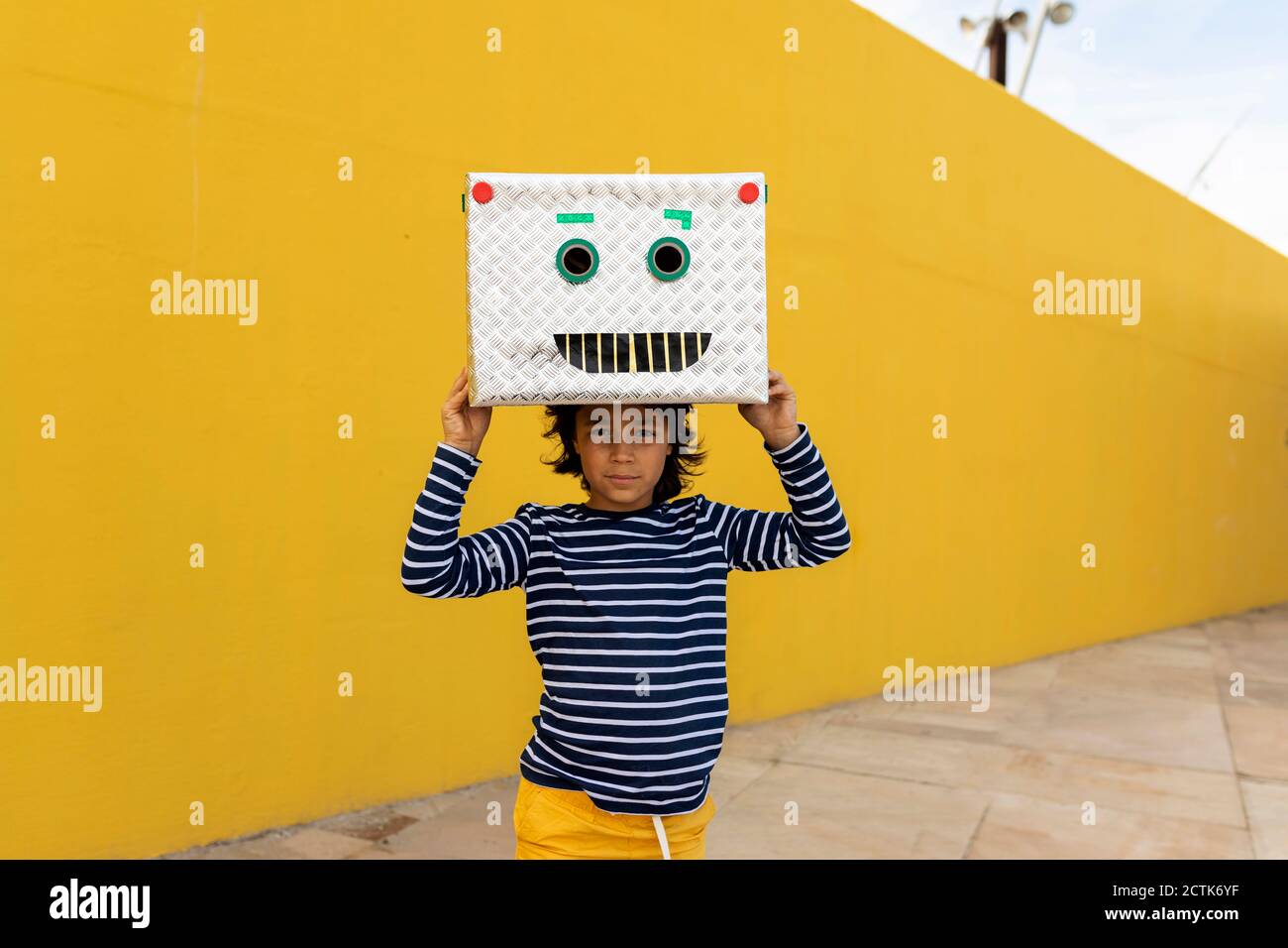 Boy wearing robot mask while standing against yellow wall Stock Photo ...