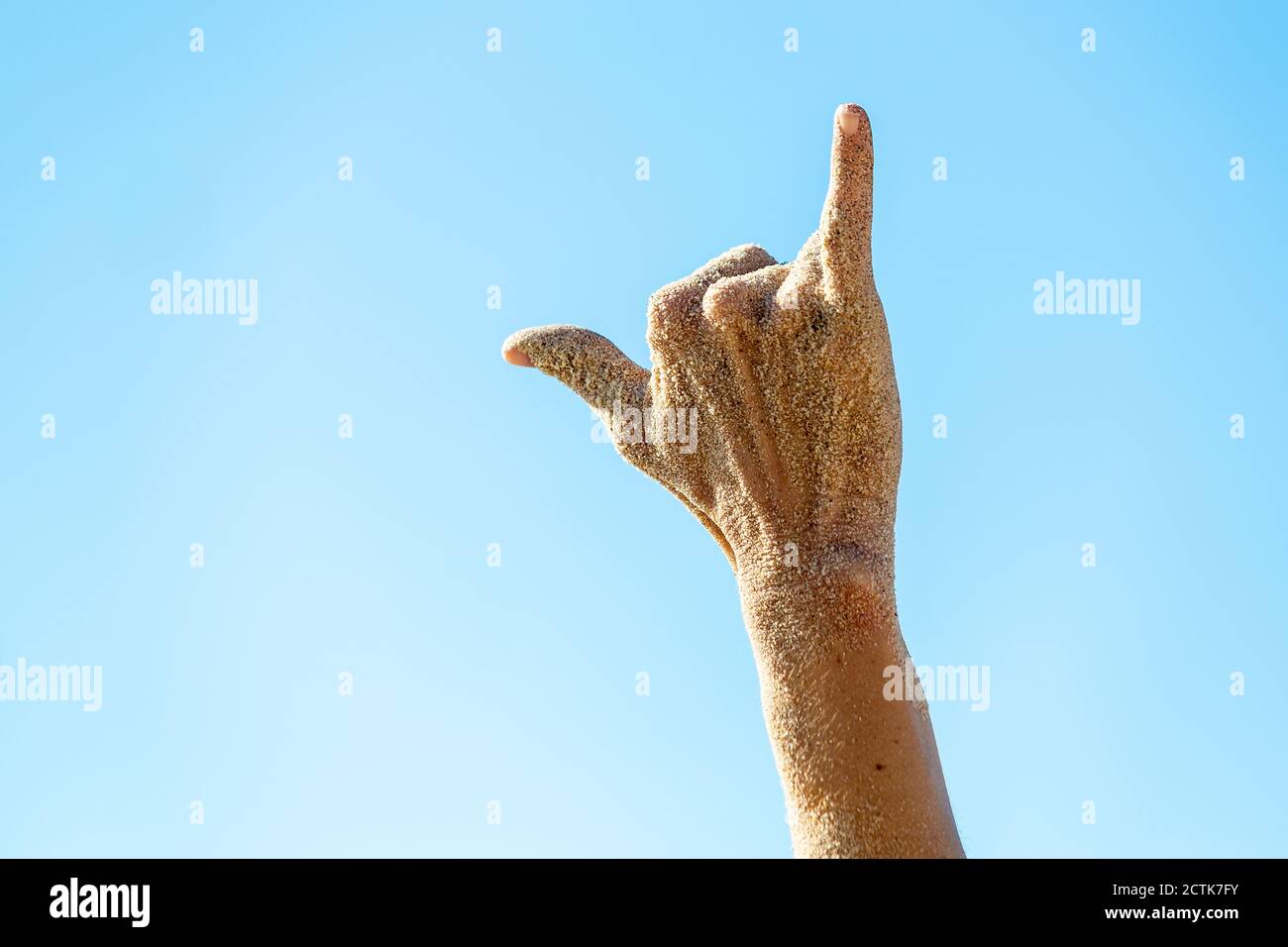 Sand-covered hand of young woman making hand sign against clear blue ...