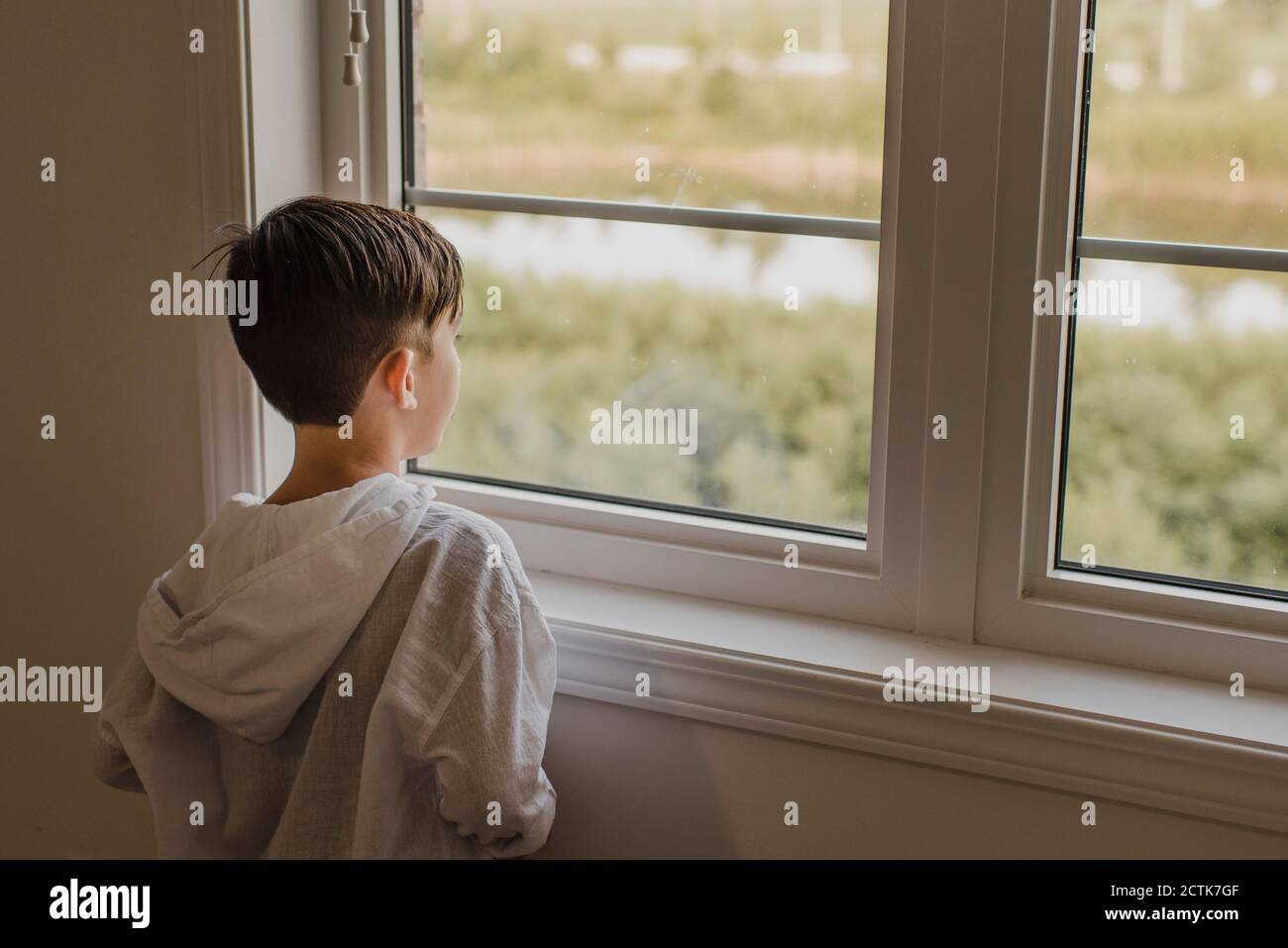 Boy looking through window while standing at home Stock Photo - Alamy