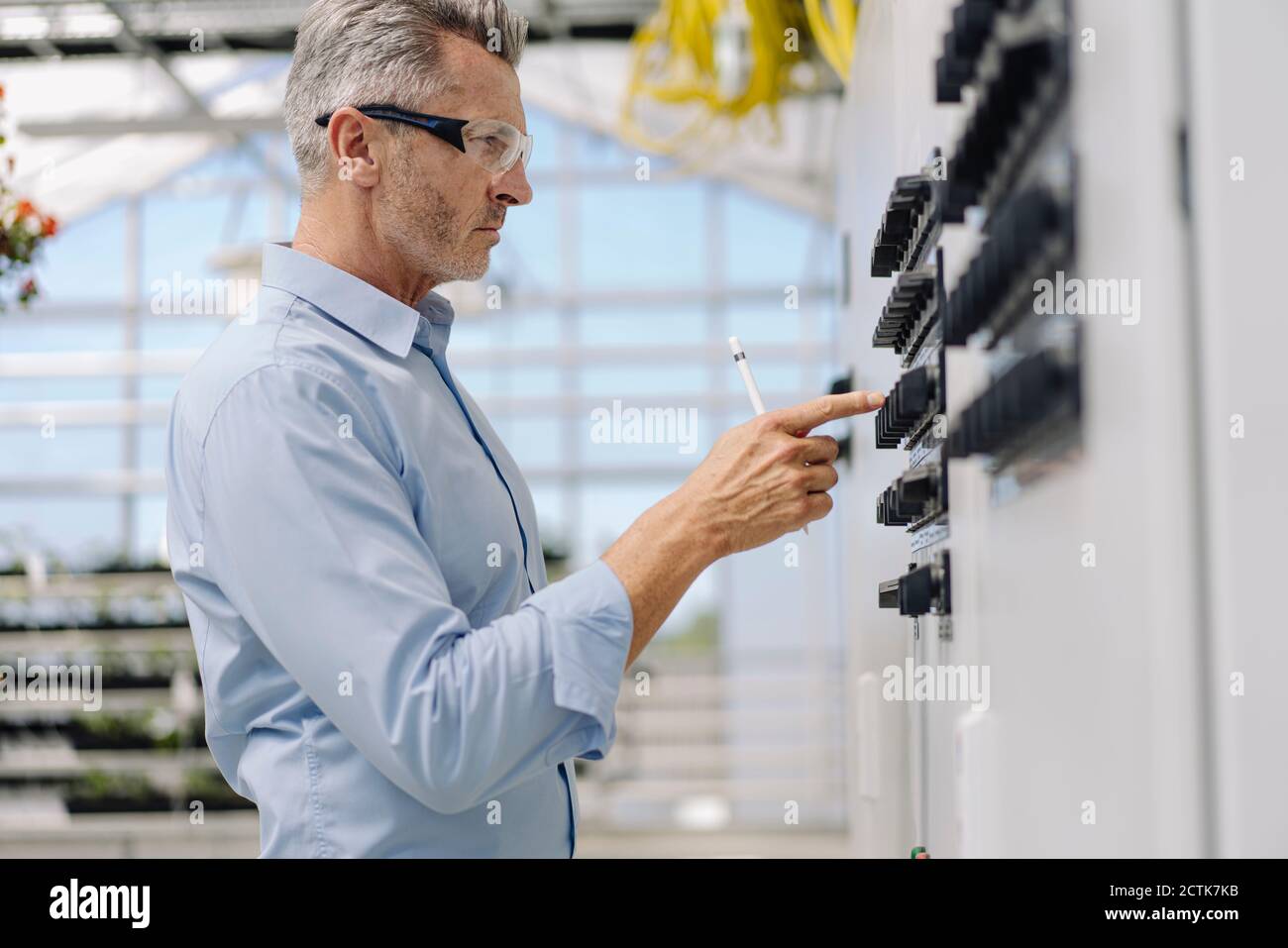 Male professional operating control panel while standing in greenhouse ...