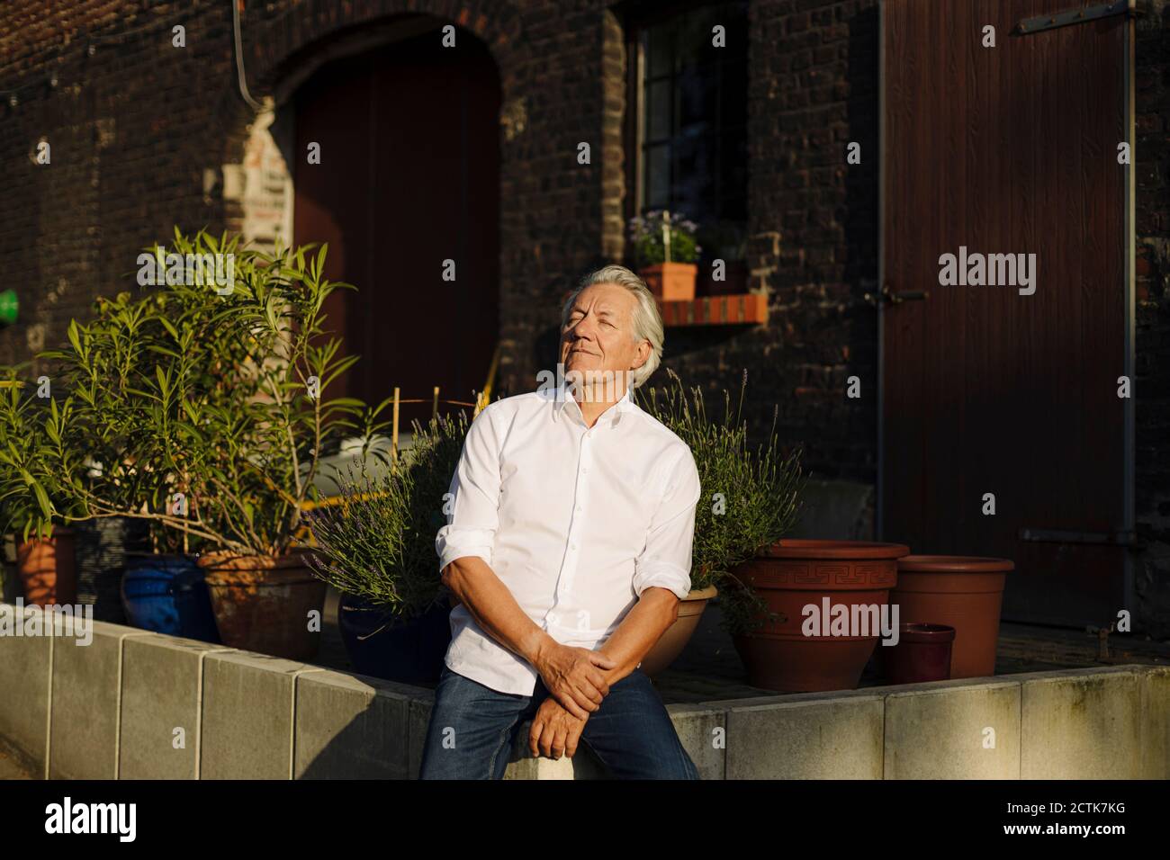 Contemplating man with eyes closed sitting on retaining wall in yard ...