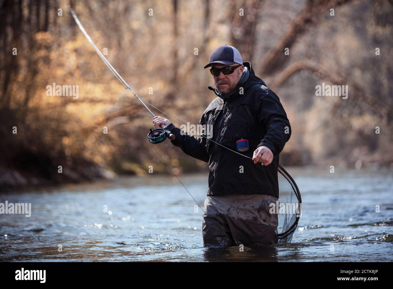 Fly fisherman holding fishing rod while standing in river at forest ...