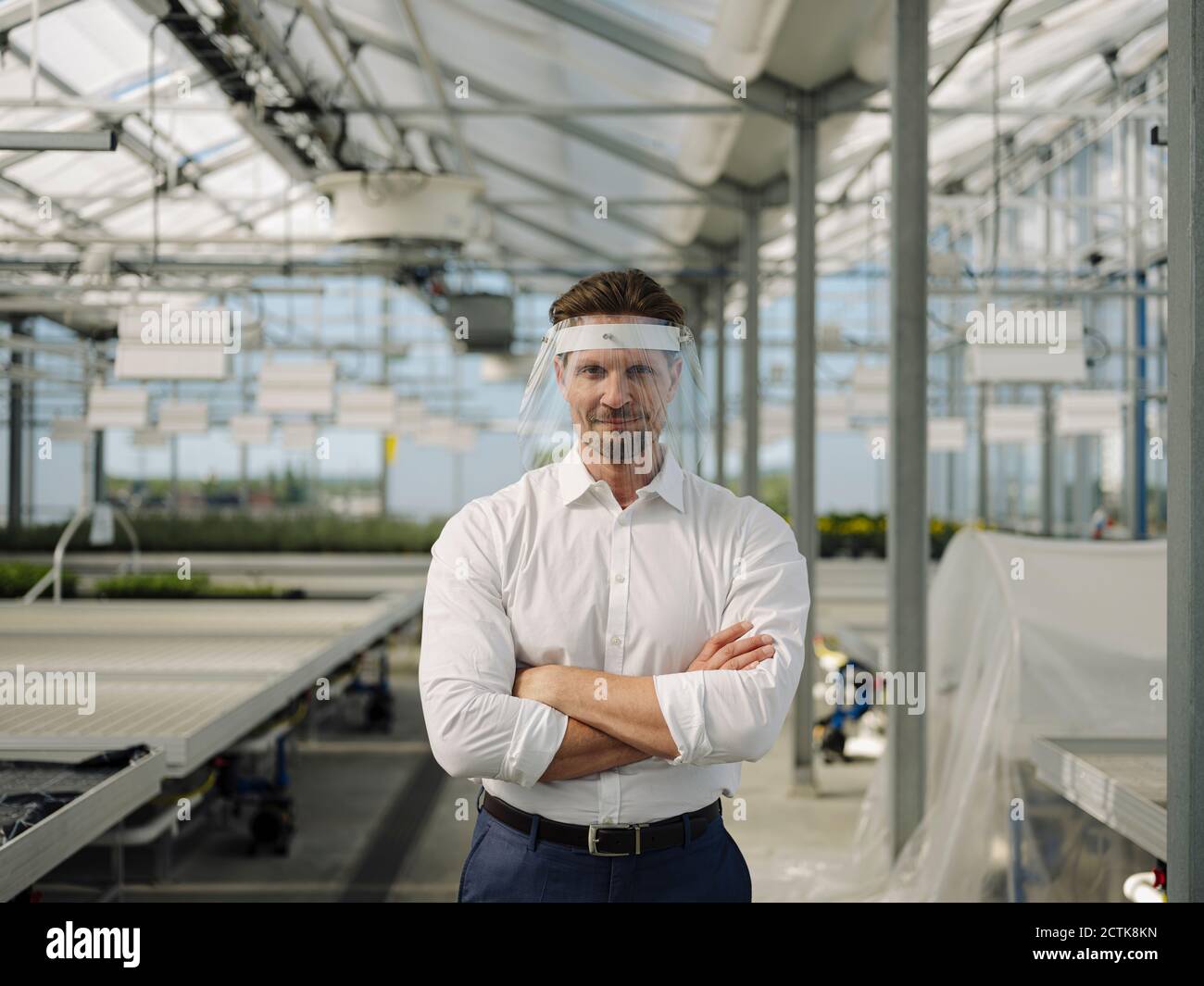 Businessman with arms crossed wearing face shield while standing in ...