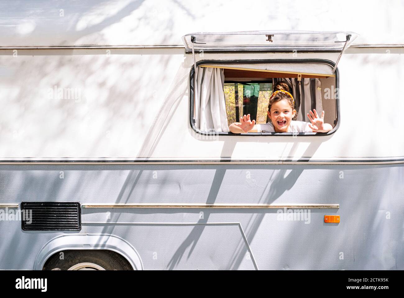 Cheerful girl screaming while looking through window of motor home ...
