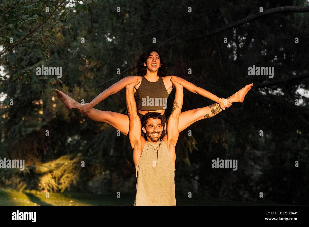 Smiling man lifting woman while practicing acroyoga in public park ...