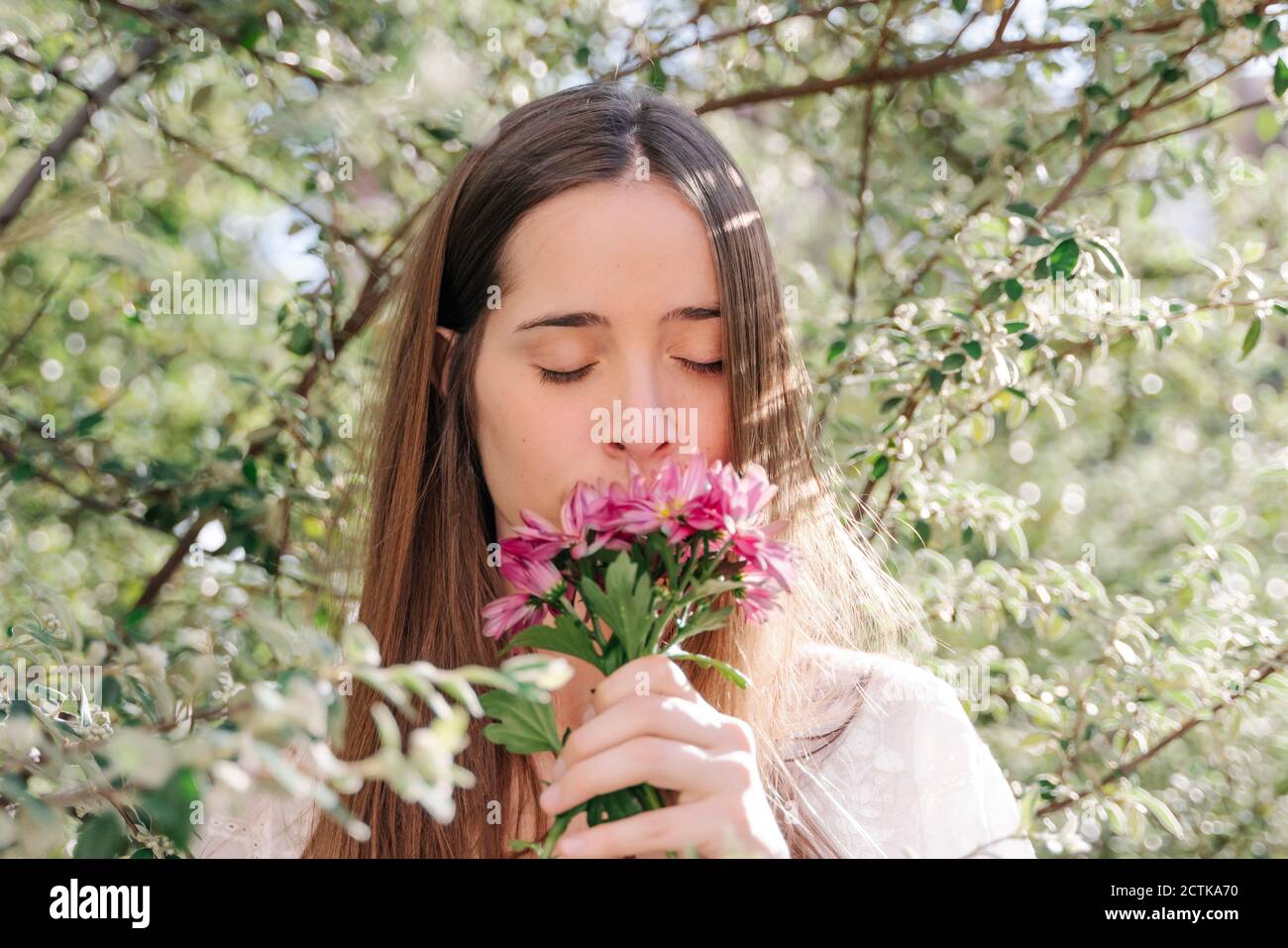 Woman smelling fresh pink flowers while standing in amidst tree park at ...