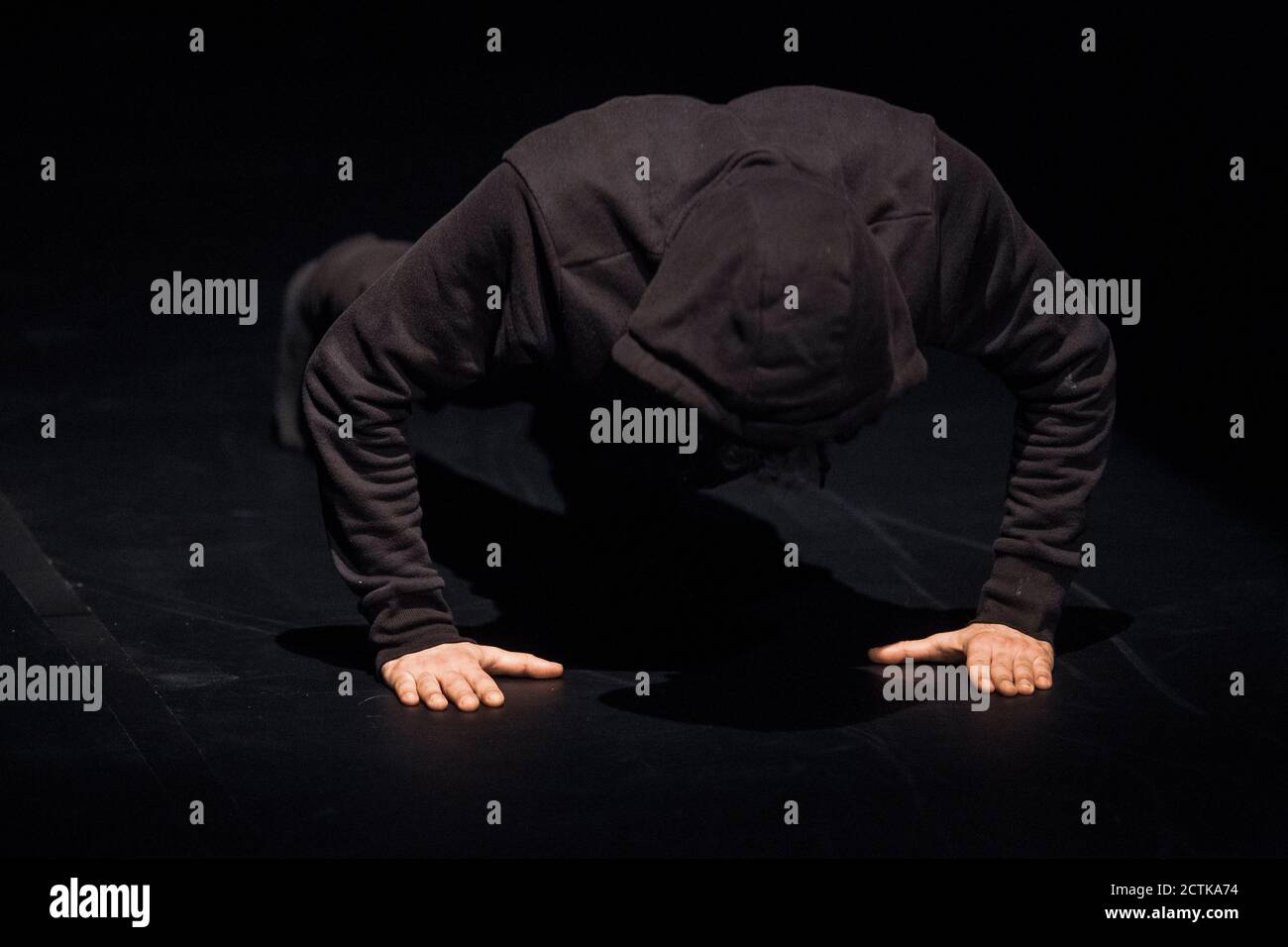 Dancer wearing black hood crouching on stage Stock Photo - Alamy