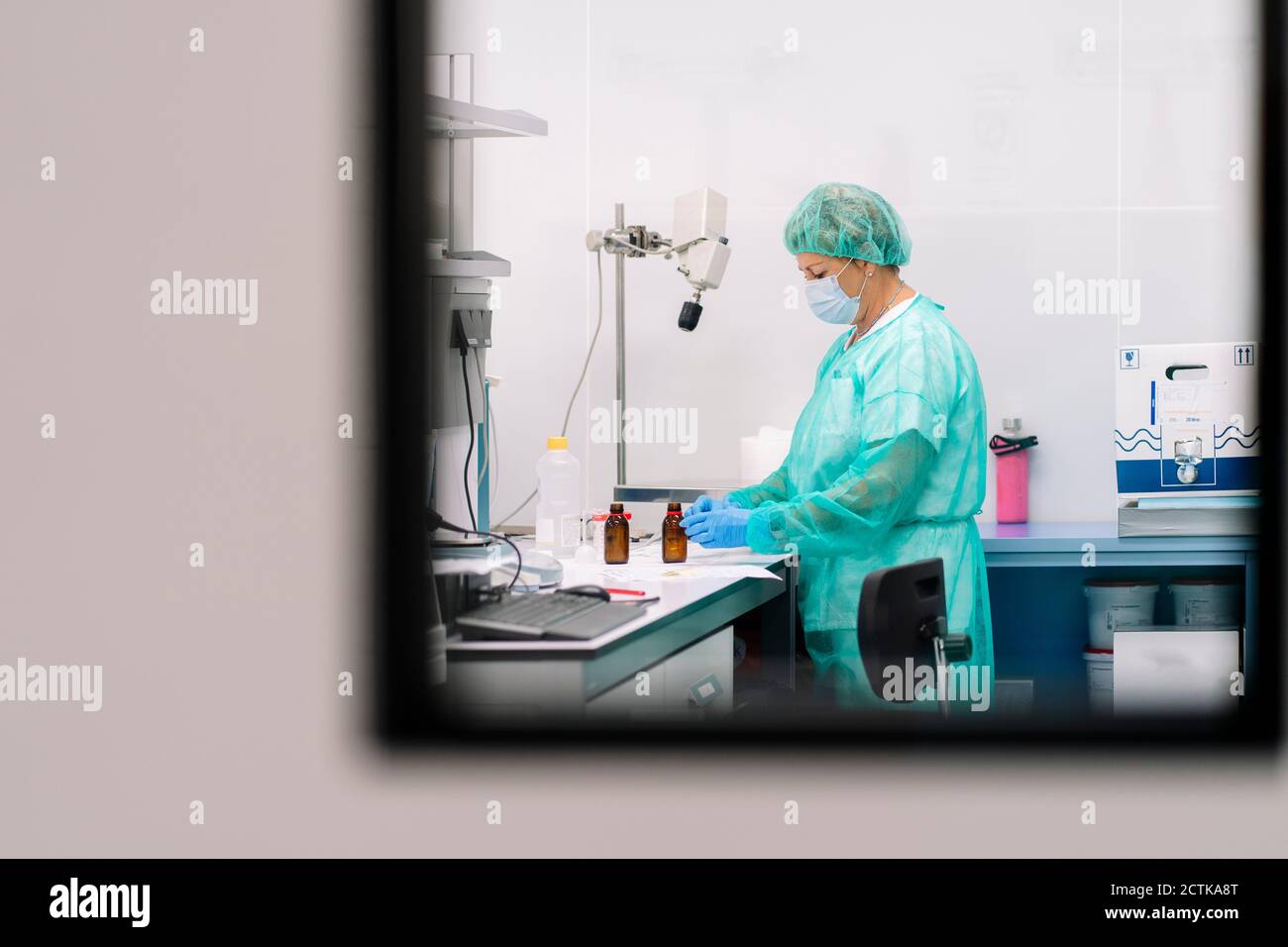 Female scientist working at table in laboratory seen through window ...