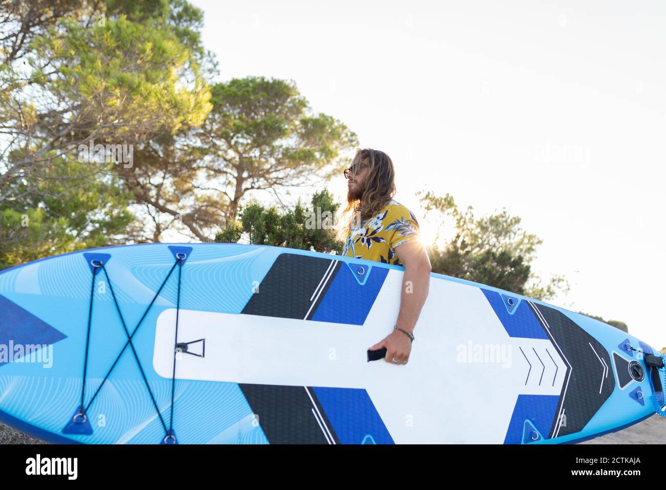 Young man carrying paddleboard at beach during sunset Stock Photo - Alamy